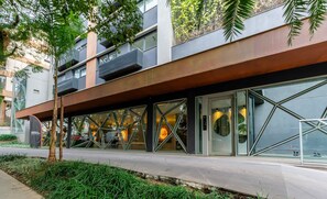 Um edifício moderno com fachada de vidro, área de estar ao ar livre e uma combinação de vegetação e elementos arquitetônicos.