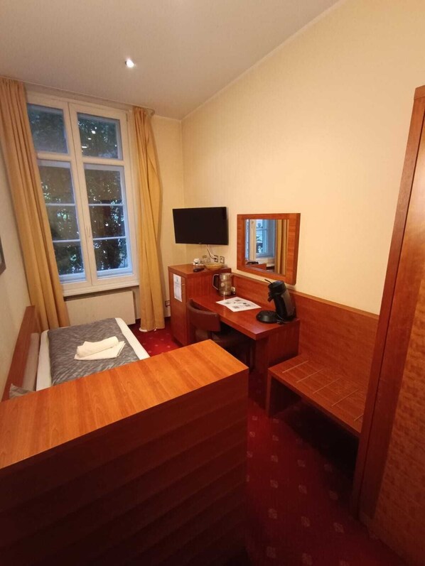 Quarto de hotel com cama, escrivaninha, cadeira, televisão e janela com cortinas.