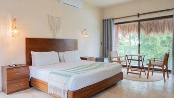 Quarto de hotel com uma cama grande, mesas de cabeceira, escrivaninha, cadeira, janela com cortinas e ar condicionado.