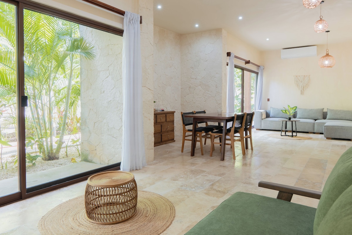 Uma sala ampla com mesa de jantar, cadeiras, sofá e uma grande janela com cortinas.