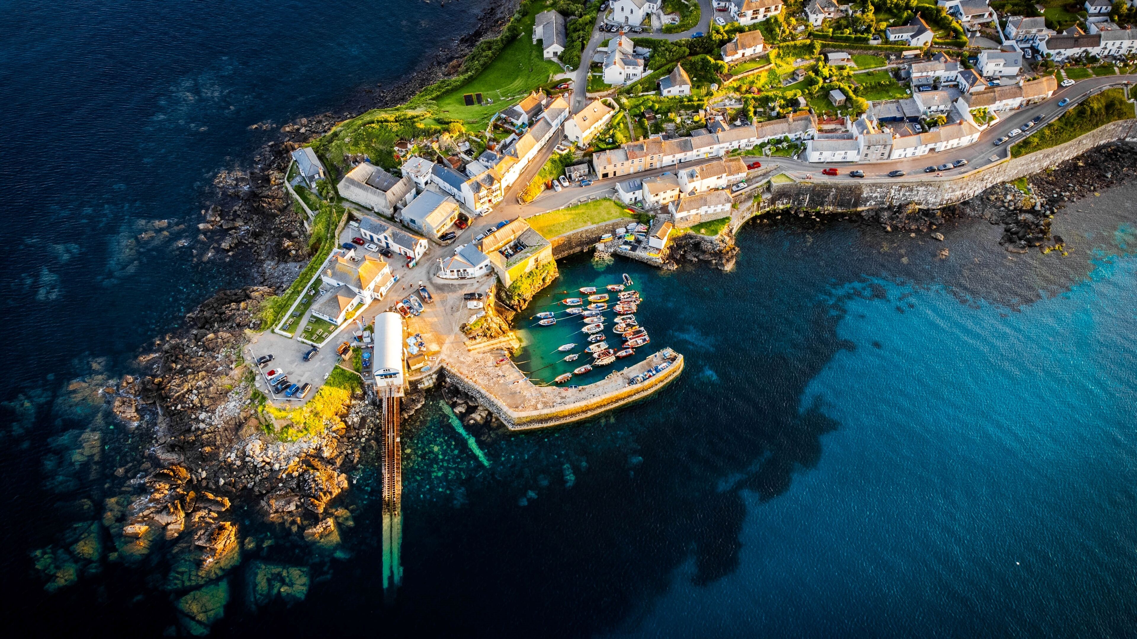 Vista aérea de uma vila costeira com um porto de iates, casas e um farol.