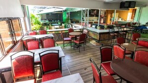 Um restaurante com cadeiras estofadas em vermelho, mesas com tampo de mármore e um espaço de bar.
