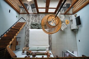 Um interior moderno com escada, cama com almofadas, luminária de fibra natural e televisão de tela plana.