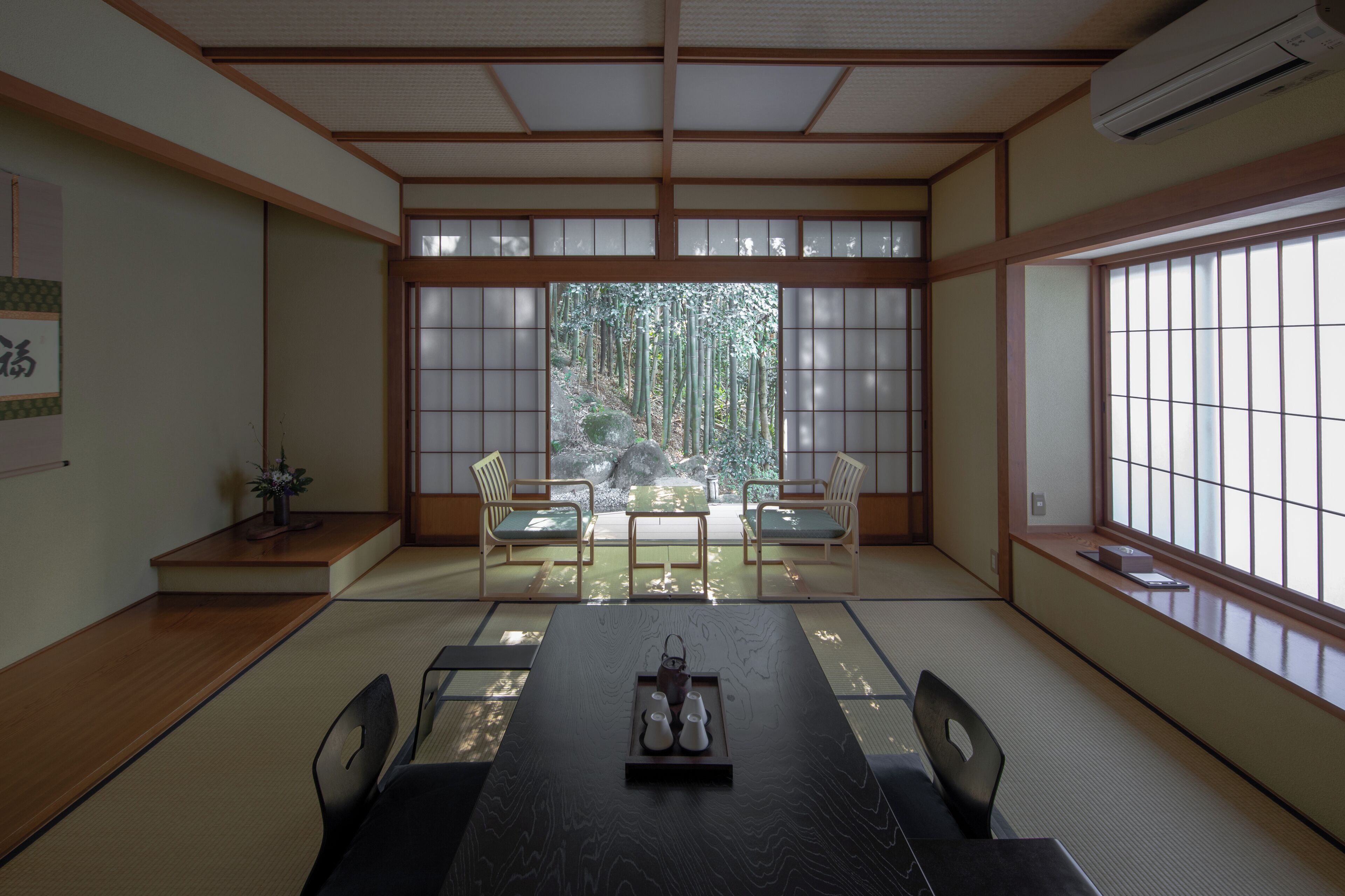 Um quarto japonês tradicional com tatames, uma mesa baixa com bandeja e portas deslizantes que dão para uma vista de uma floresta de bambu.