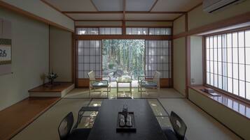 Um quarto japonês tradicional com tatames, uma mesa baixa com bandeja e portas deslizantes que dão para uma vista de uma floresta de bambu.