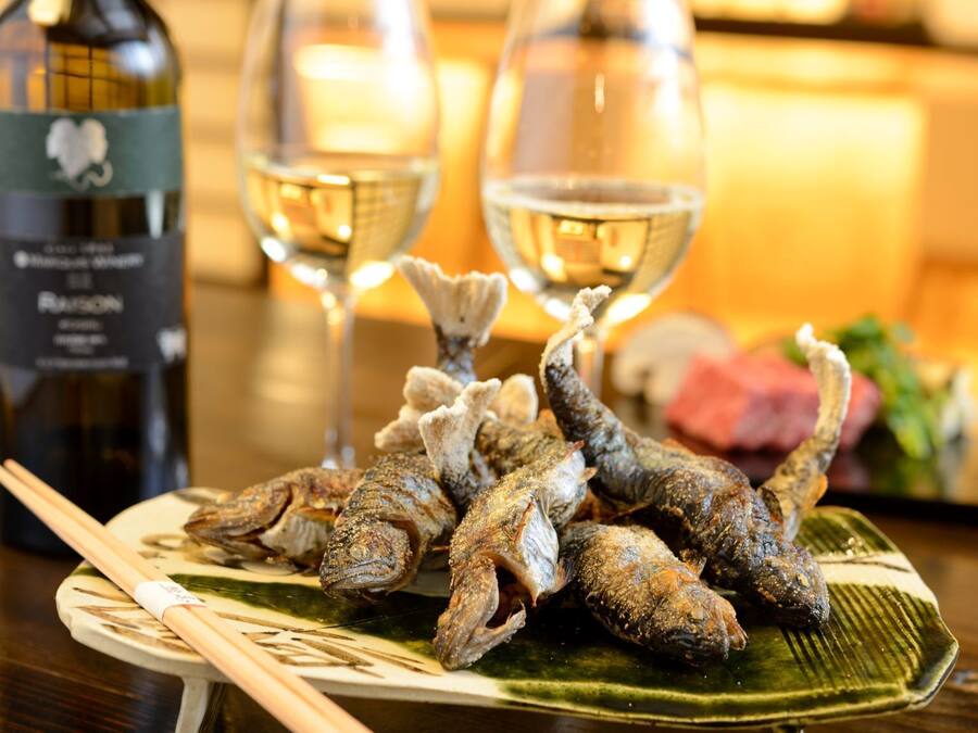 Prato de peixe frito com pauzinhos e uma garrafa de vinho sobre uma mesa.
