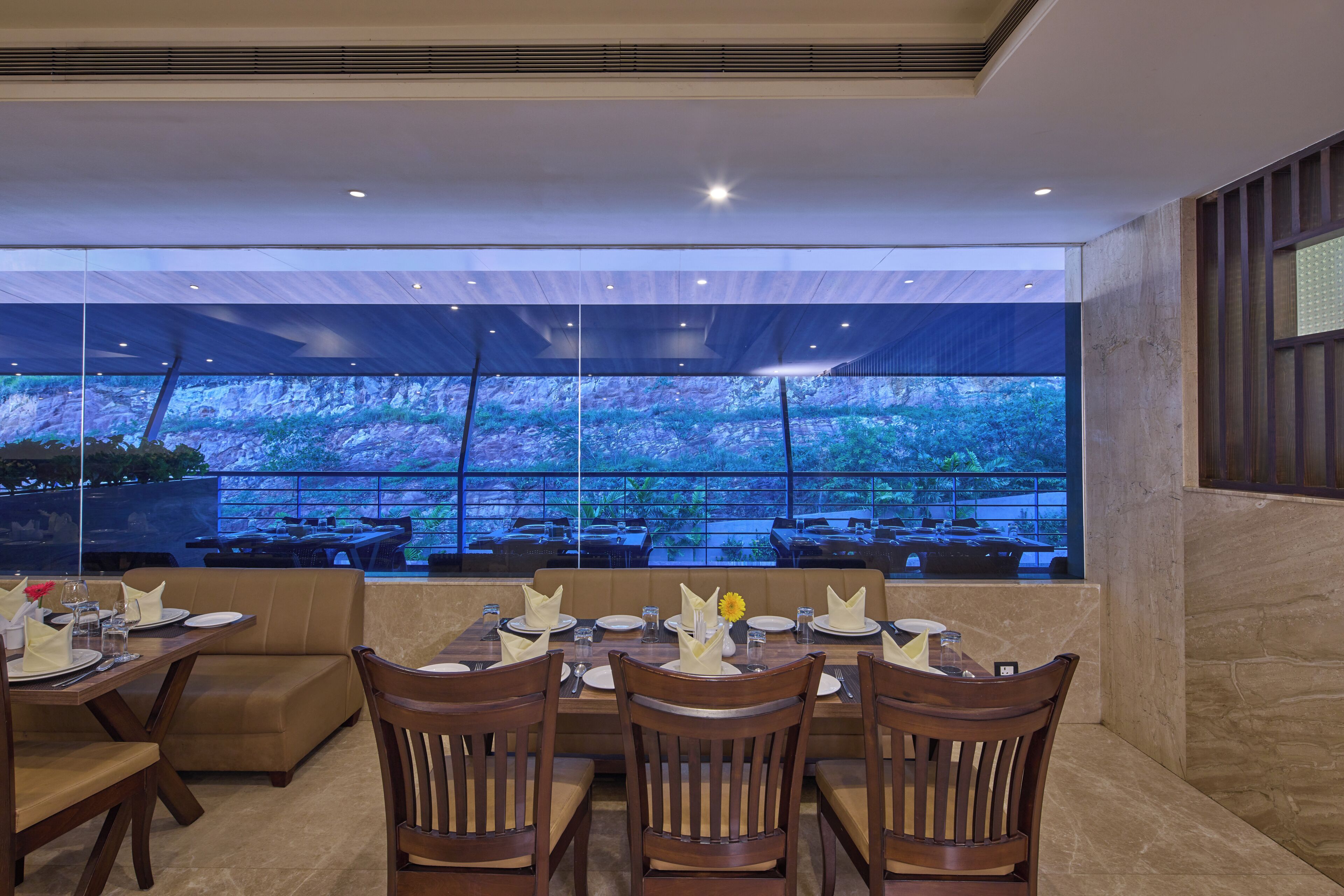 Restaurante com vista para uma paisagem rochosa através de amplas janelas. Mesas dispostas com pratos, copos e talheres.