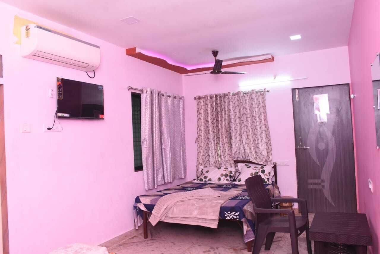 Quarto com cama, cadeira, mesa, ar condicionado, ventilador de teto e televisão.