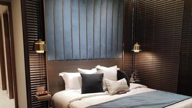 Quarto moderno com uma cama grande, cabeceira de madeira, mesas de cabeceira e um criado-mudo com abajur.