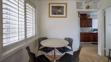 Uma sala de jantar com uma mesa redonda e quatro cadeiras, um quadro na parede e uma cozinha ao fundo.
