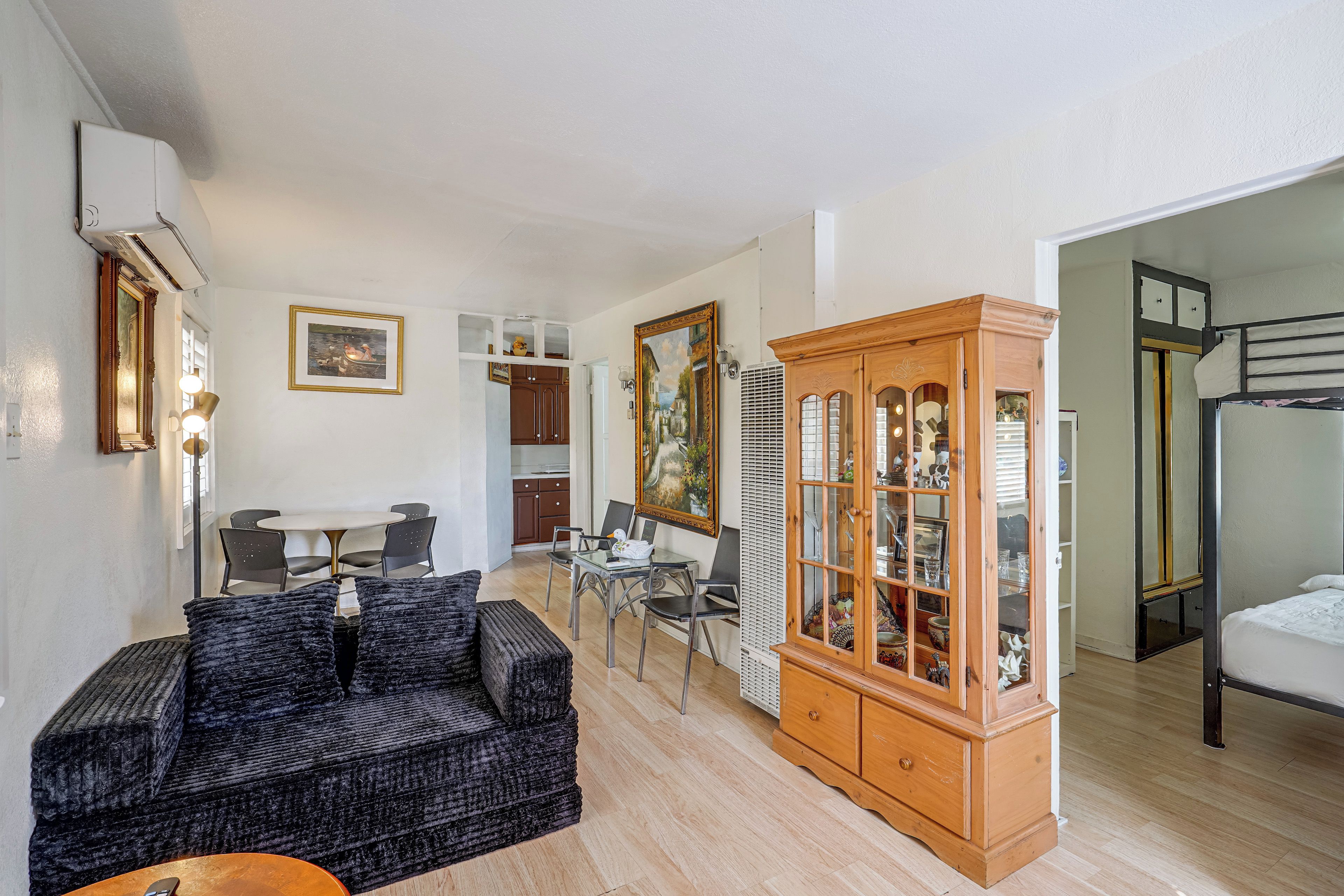 Uma sala de estar mobiliada com sofá, mesa de jantar com cadeiras, aparador com portas de vidro e uma cama beliche.