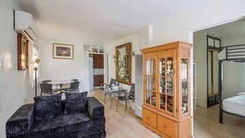 Uma sala de estar mobiliada com sofá, mesa de jantar com cadeiras, aparador com portas de vidro e uma cama beliche.
