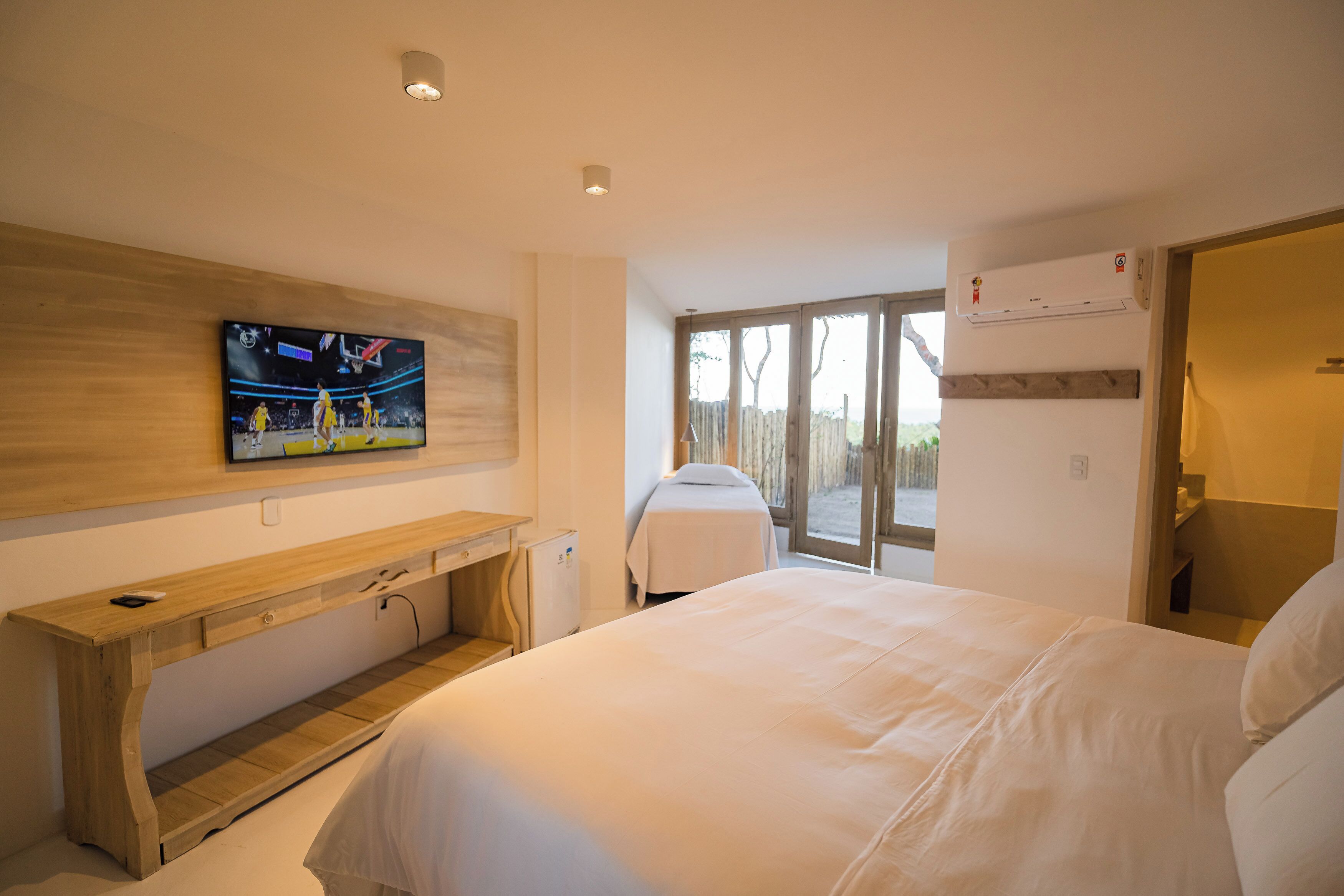Quarto de hotel com cama, televisão fixada na parede, secretária e janela com vista para o exterior.