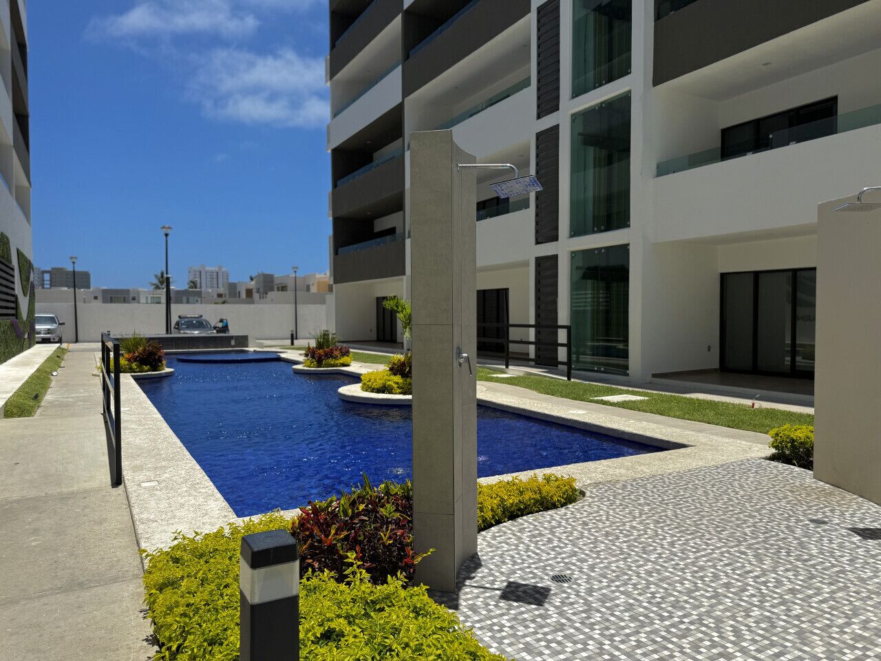 Um edifício moderno com piscina, cercado por vegetação e um caminho de azulejos.