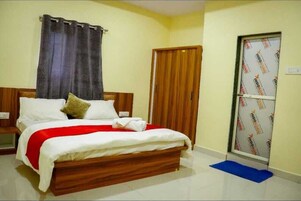 Quarto com cama de madeira, roupa de cama branca, um cobertor vermelho, guarda-roupa de madeira e uma porta com isolamento.
