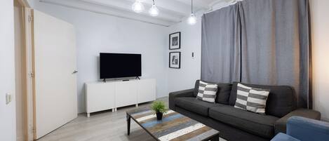 Uma sala de estar moderna com uma televisão de tela plana, um sofá com almofadas, uma mesa de centro listrada e um lustre.