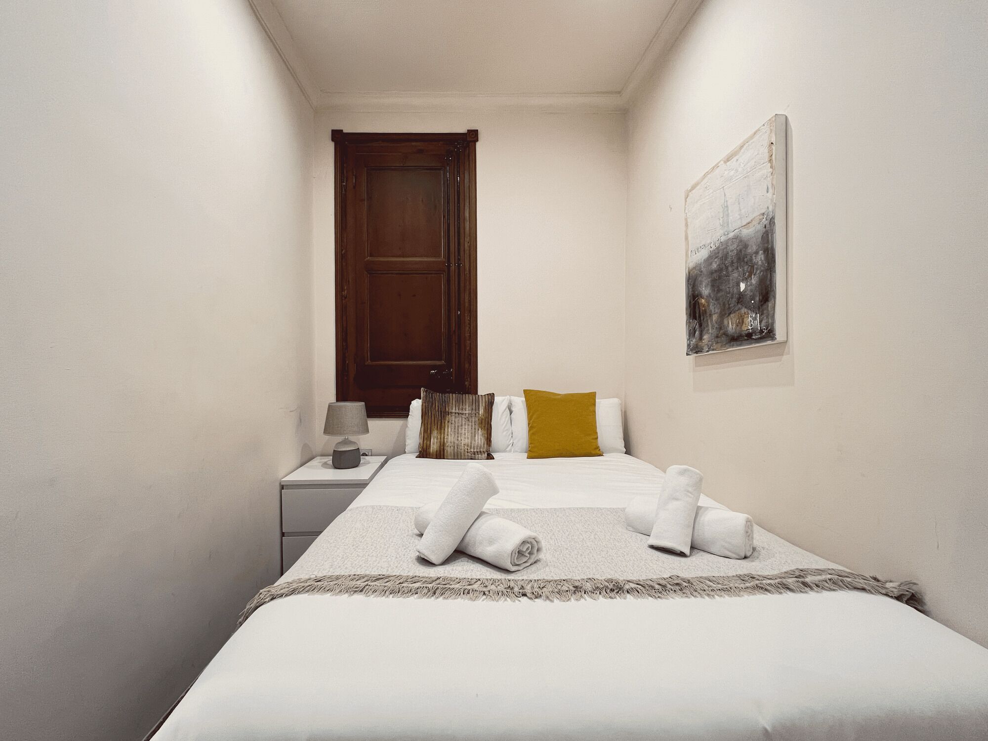 Quarto bem arrumado com cama, mesa de cabeceira, luminária e um quadro na parede.