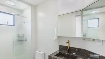 Um banheiro moderno com box de vidro, pia de mármore e detalhes dourados, e um espelho grande.