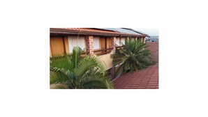 Um edifício com telhado de telhas vermelhas, paredes de tijolos e uma varanda com plantas de palmeira.