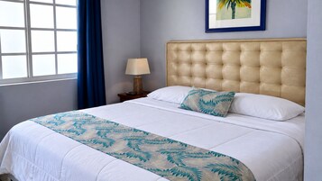 Quarto de hotel com uma cama grande, cabeceira, mesa de cabeceira com abajur e um quadro na parede.
