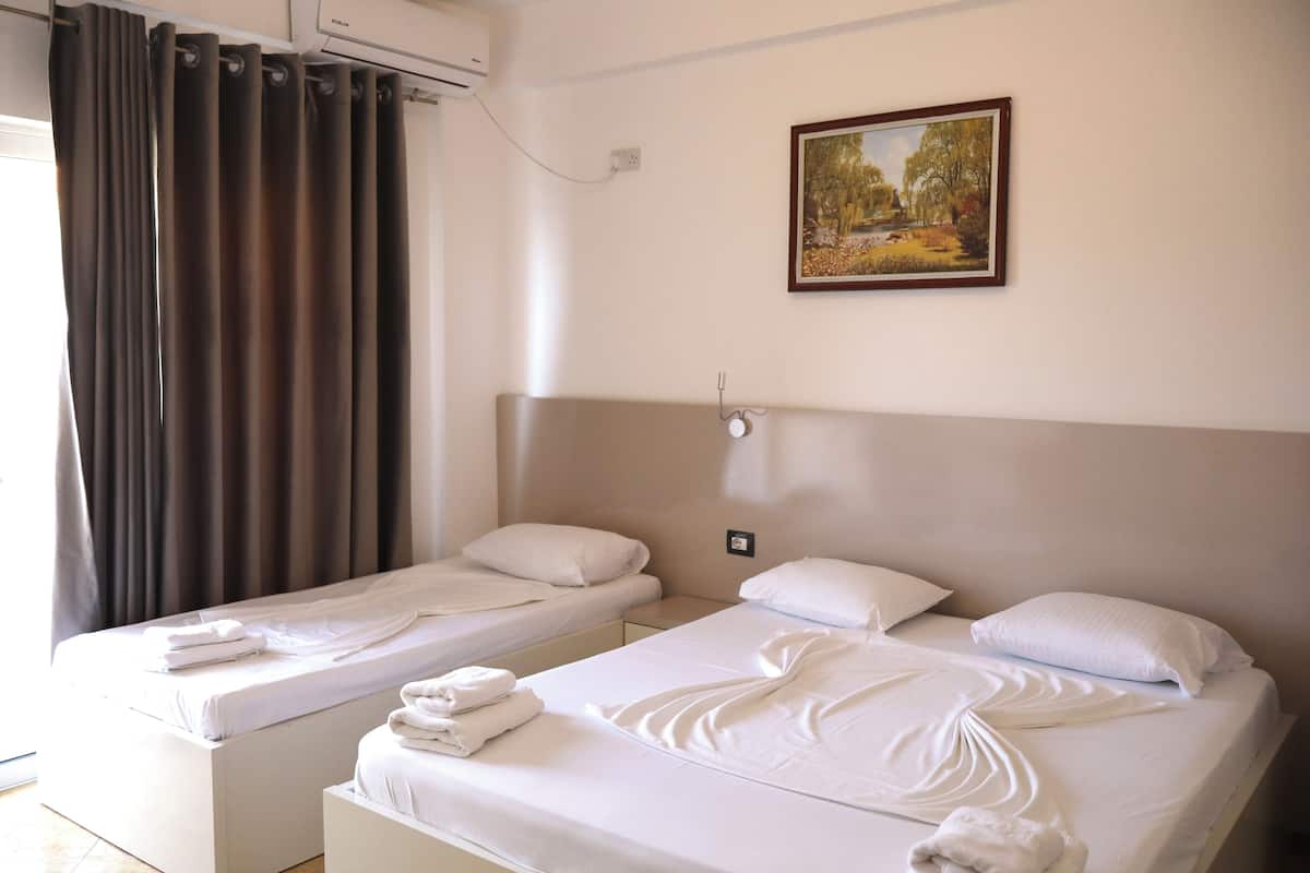 Quarto de hotel com duas camas de solteiro, um quadro na parede e uma janela com cortinas.