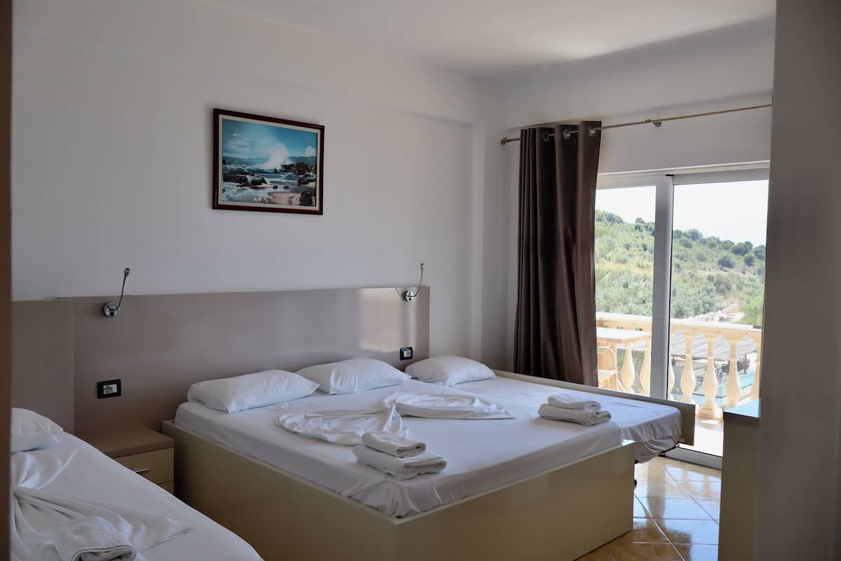 Quarto de hotel com uma cama grande, um quadro na parede e vista para uma varanda com piscina.