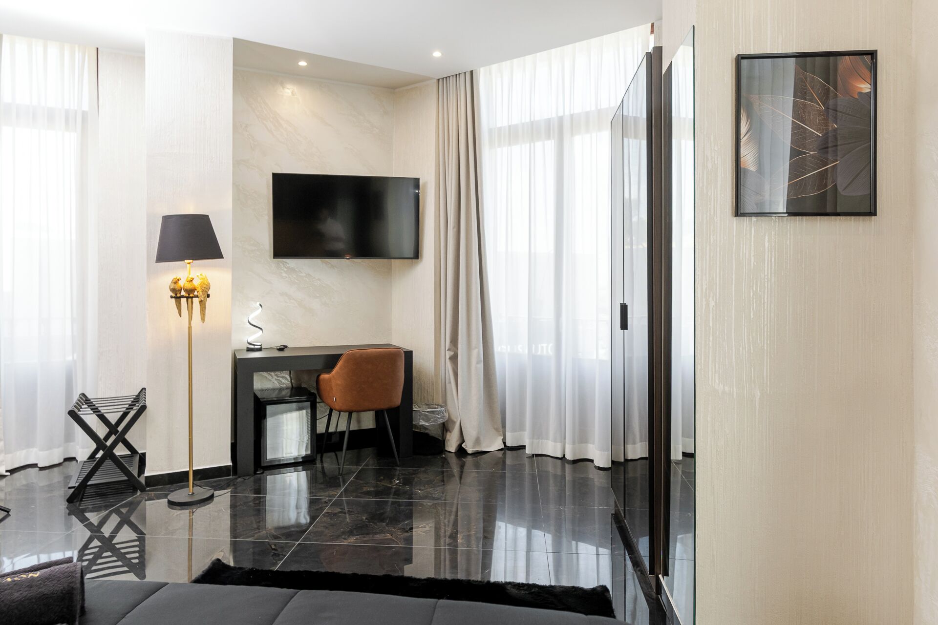 Quarto de hotel moderno com televisão de tela plana, escrivaninha com cadeira, abajur e uma grande janela com cortinas leves.
