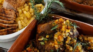 Buffet com diversos pratos, incluindo carnes assadas, batatas e uma decoração de abacaxi.