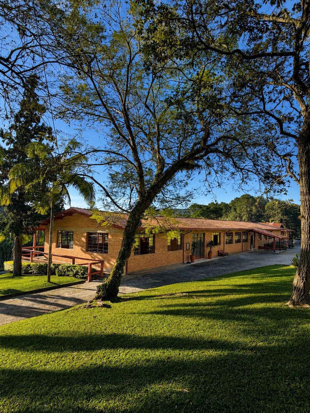 Um edifício de dois andares com telhado de telhas vermelhas, entrada com calçada e gramado bem cuidado.