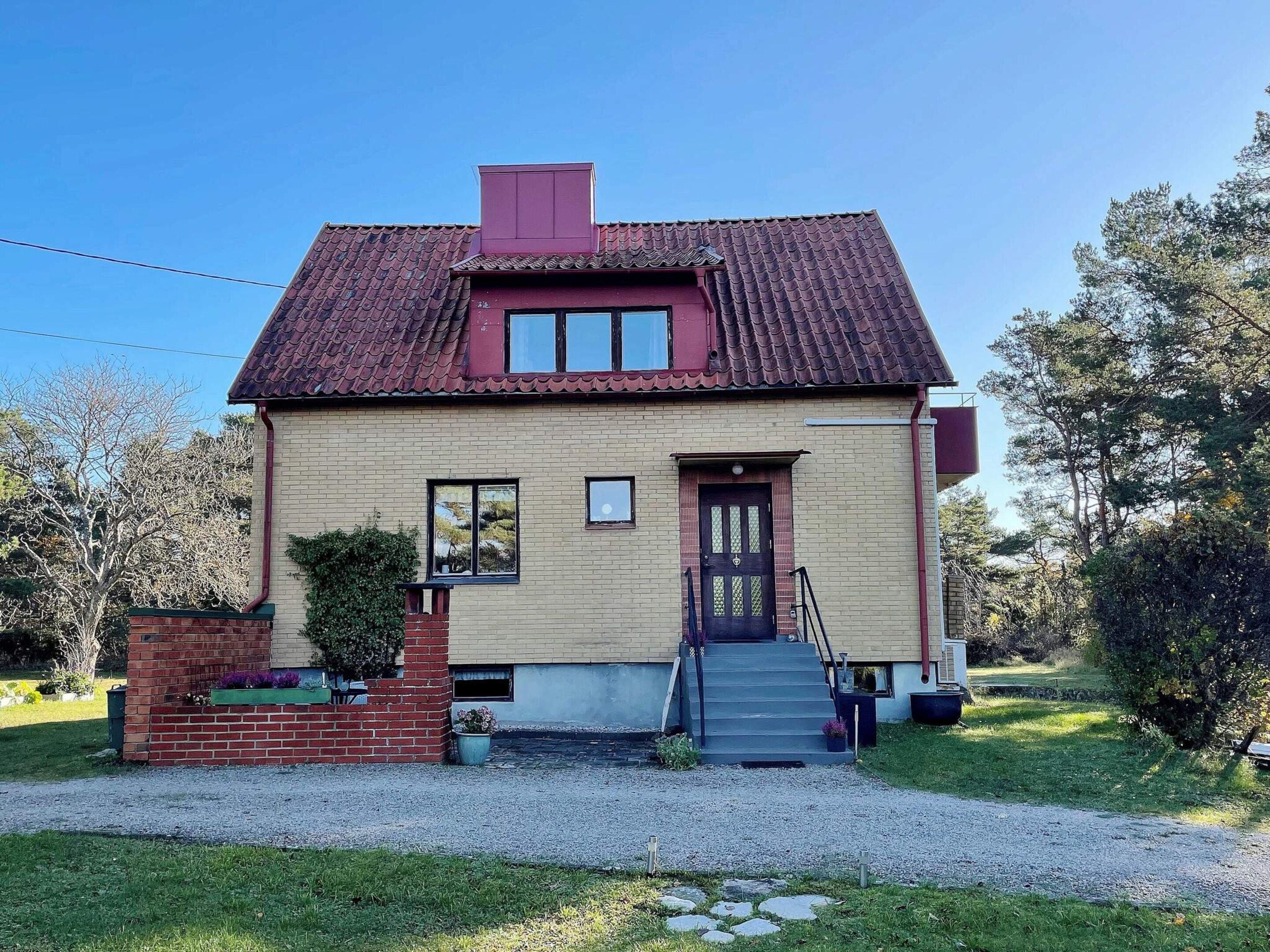 Uma casa de dois andares com telhado de telhas vermelhas, fachada de tijolo e entrada frontal com porta e janelas.