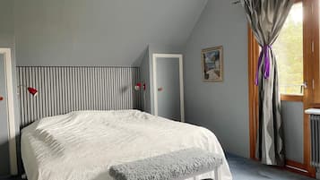 Quarto com cama, um banquinho, um quadro e janela com cortinas.