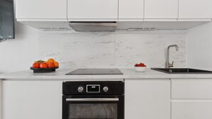 Cozinha moderna com armários brancos, forno preto, pia de aço inoxidável e backsplash de mármore.