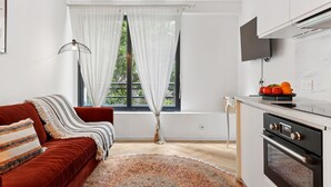 Uma cozinha moderna com forno embutido, sala de jantar com sofá vermelho e uma janela grande com cortinas leves.