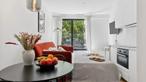Uma cozinha moderna com armários brancos, um espaço de refeições com mesa e cadeiras, um sofá vermelho e uma janela grande com vista para o verde.