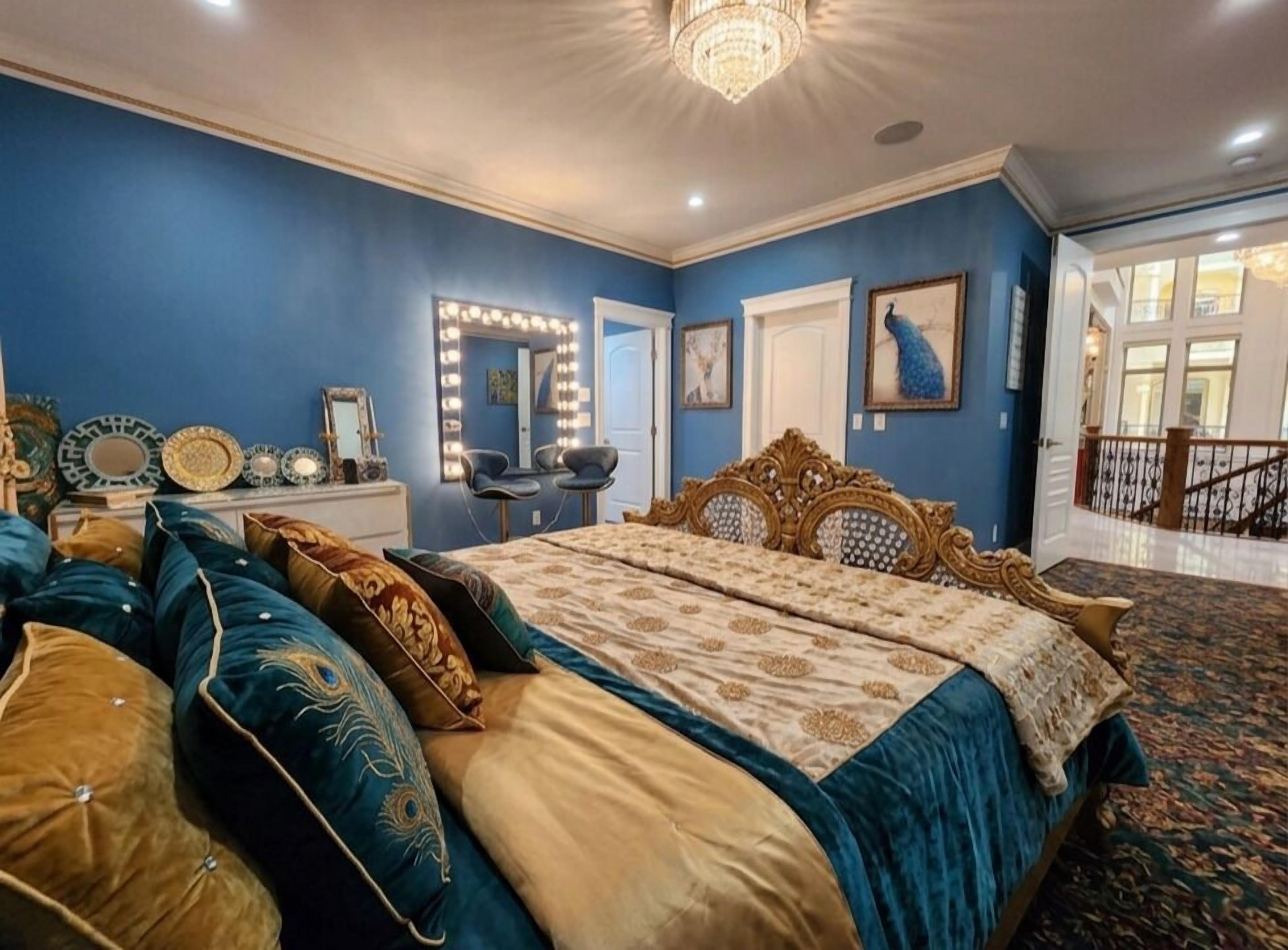 Quarto com uma cama grande, toucador iluminado, pintura de pavão e escada que leva a outro cômodo.