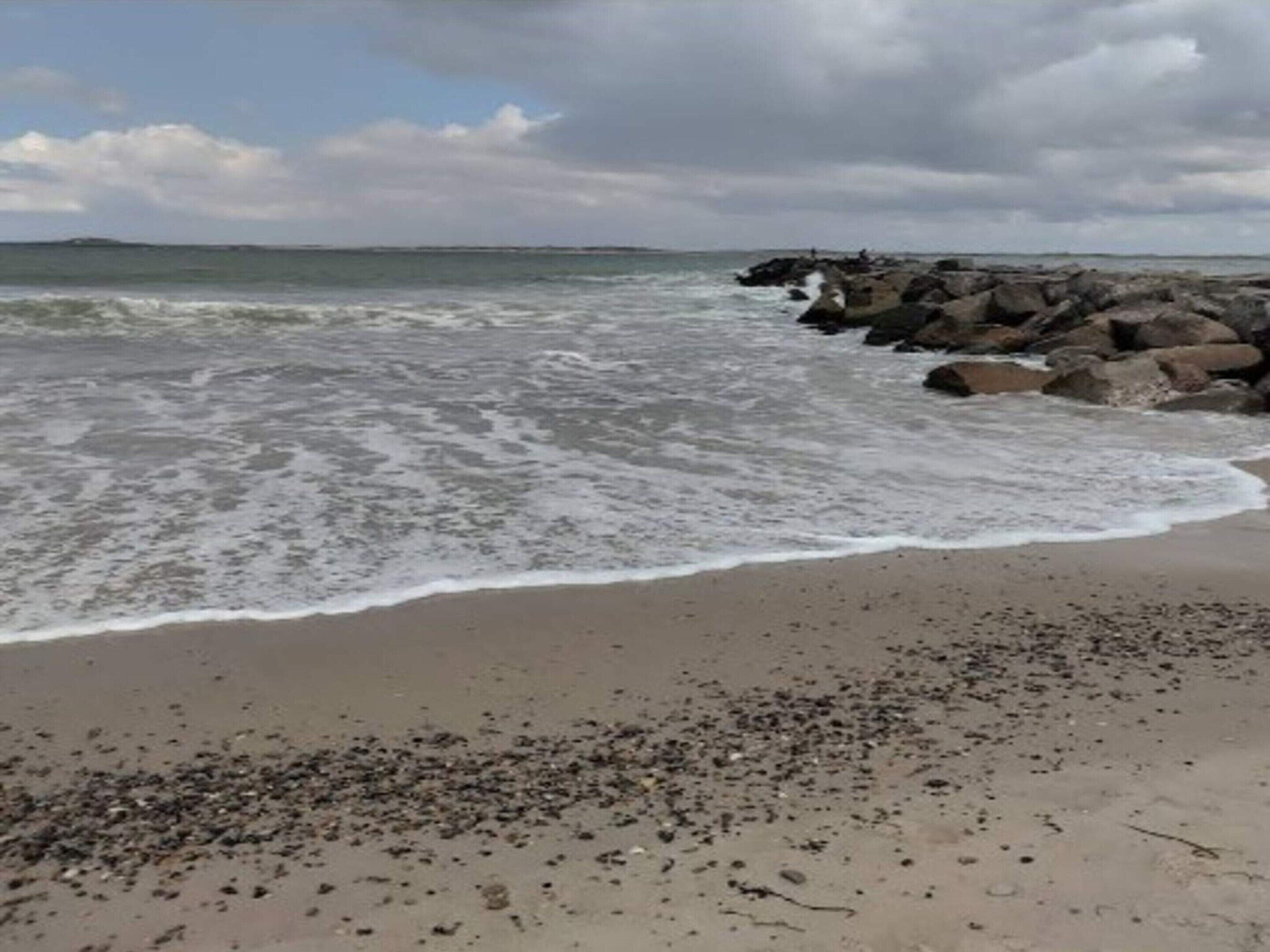 Uma praia com ondas, pedras e um litoral rochoso.