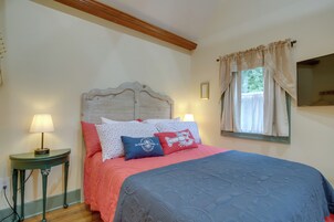 Quarto com cama, duas luminárias de cabeceira, mesa de cabeceira, janela com cortinas e televisão na parede.
