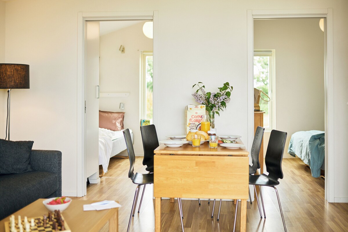 Uma sala de estar moderna com um sofá, uma mesa de jantar com cadeiras e uma mesa de centro com uma tigela e um tabuleiro de xadrez.