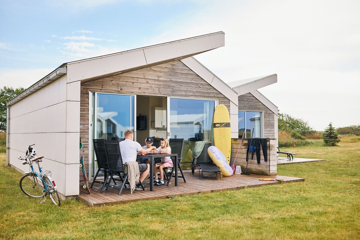 Uma casa moderna com varanda, área de refeições e uma prancha de surf.