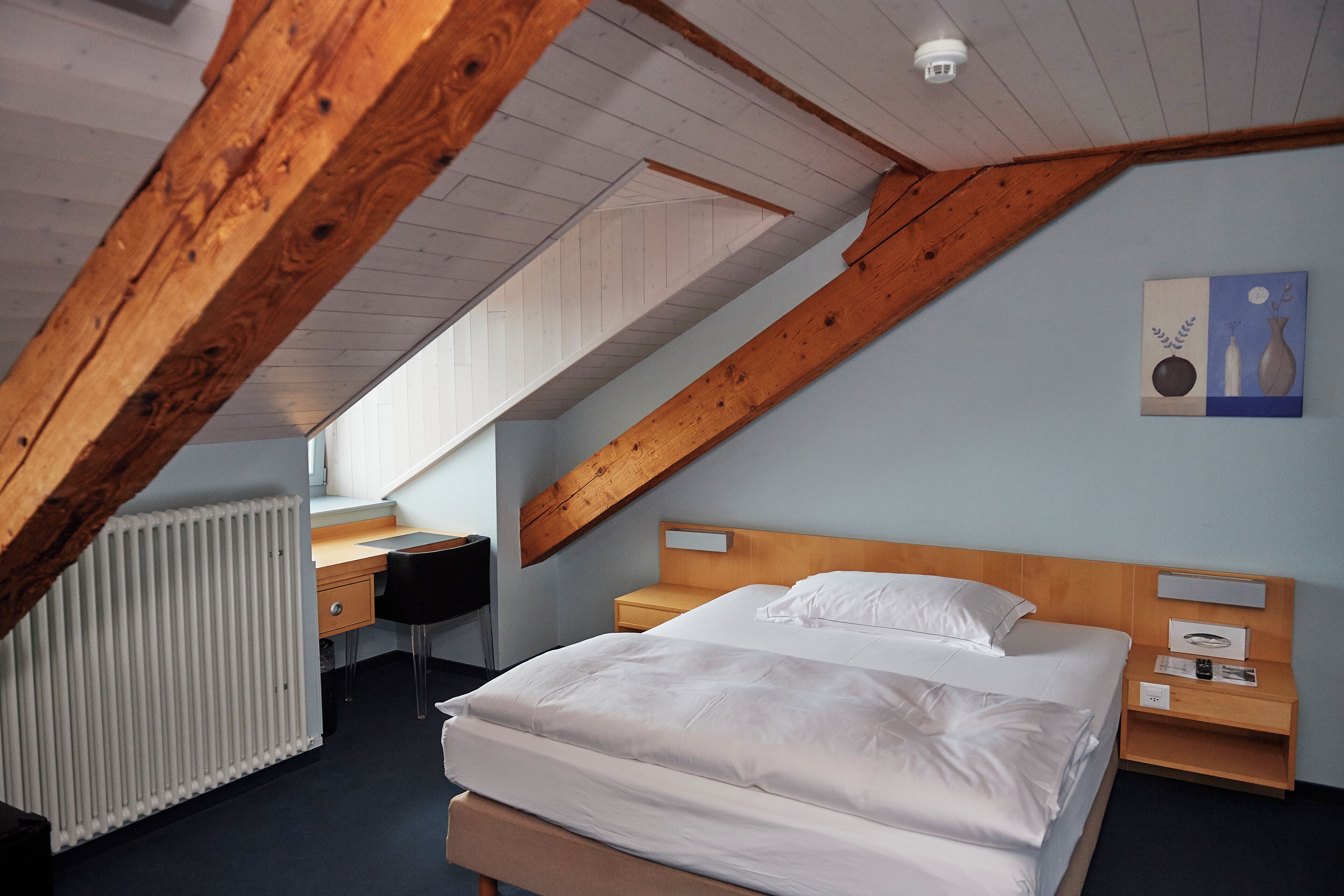 Quarto com teto de madeira, uma cama, uma escrivaninha e um radiador.