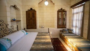 Quarto tradicional com uma cama grande, duas camas menores, um arco decorativo e uma janela com cortinas.