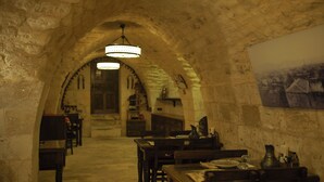 Interior com paredes de pedra, tetos em arco e mesas e cadeiras de madeira.
