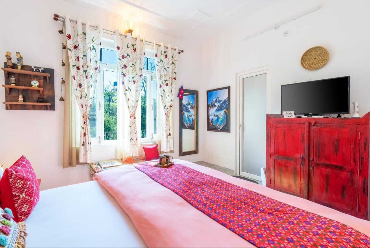 Um quarto com uma cama, um guarda-roupa vermelho, uma televisão e obras de arte na parede.