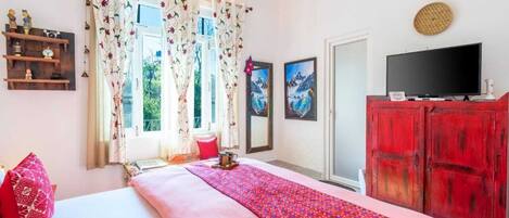 Um quarto com uma cama, um guarda-roupa vermelho, uma televisão e obras de arte na parede.