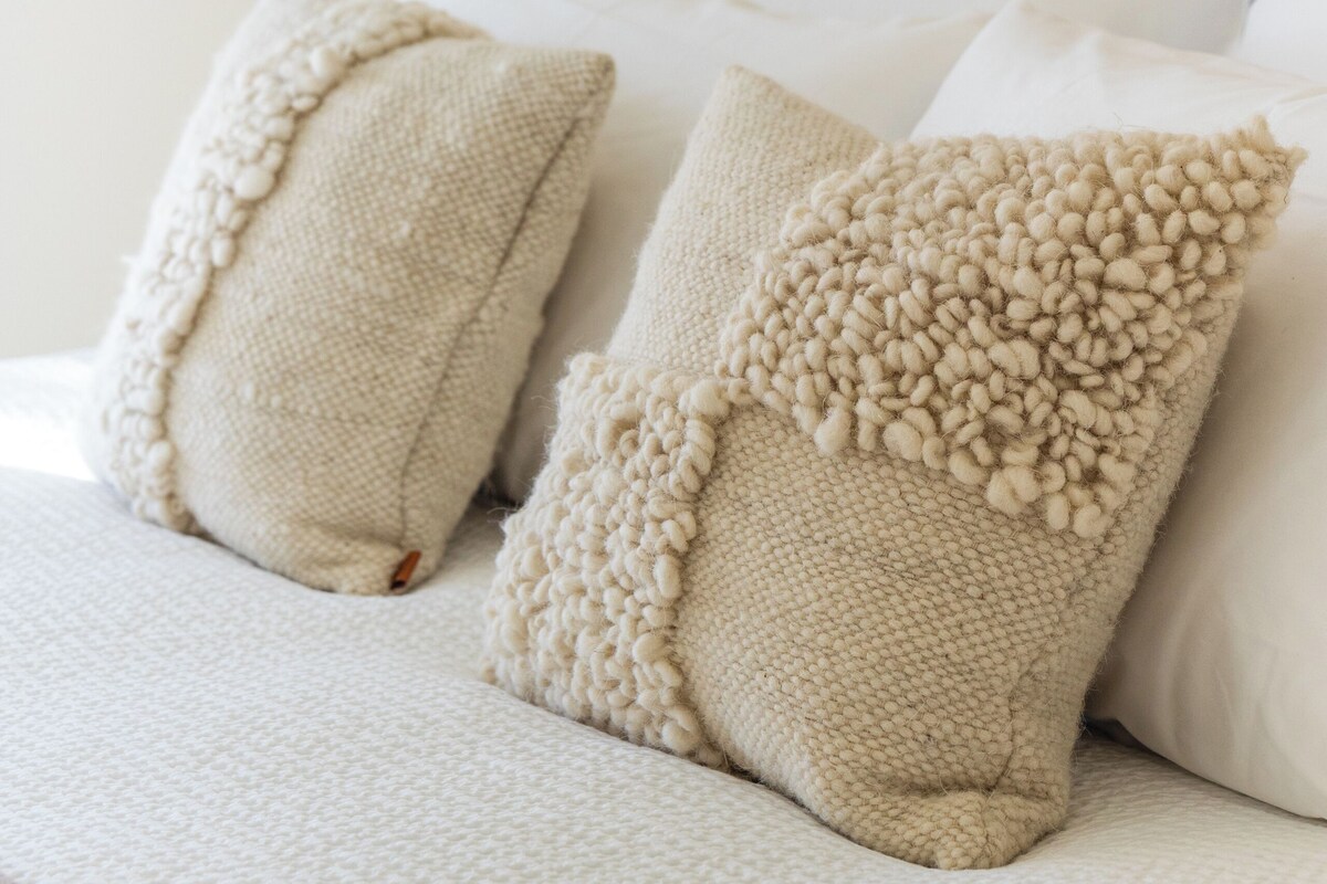 Uma cama com roupa de cama branca e duas almofadas decorativas.