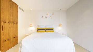 Quarto com um amplo guarda-roupa de madeira, cama com roupa de cama branca e almofadas listradas, e luminárias fixadas na parede.