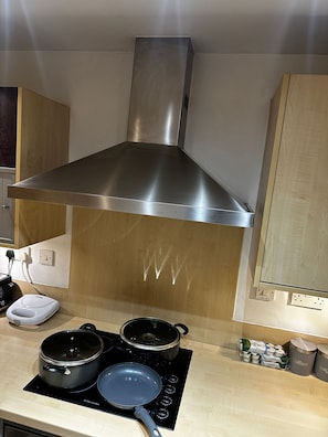 Cozinha com exaustor de aço inoxidável, fogão com panelas e uma frigideira, e uma cafeteira.
