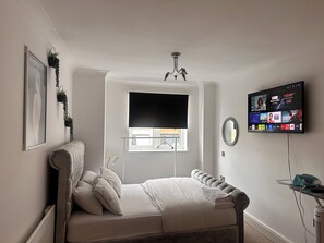 Quarto com cama, televisão na parede, janela e luminária no teto.