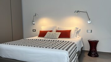 Quarto moderno com cama, duas luminárias de cabeceira, mesa de cabeceira e um vaso decorativo.