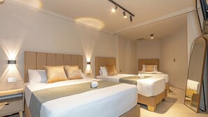 Quarto de hotel com duas camas, uma mesinha de cabeceira, um espelho e um lustre.